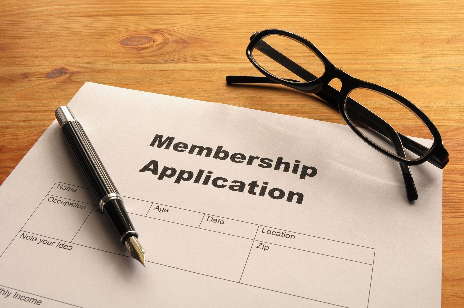A paper of a membership application, a pen and glasses on a table.